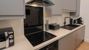 Cozinha moderna com fogão por indução preto, forno embutido, torradeira e cafeteira.
