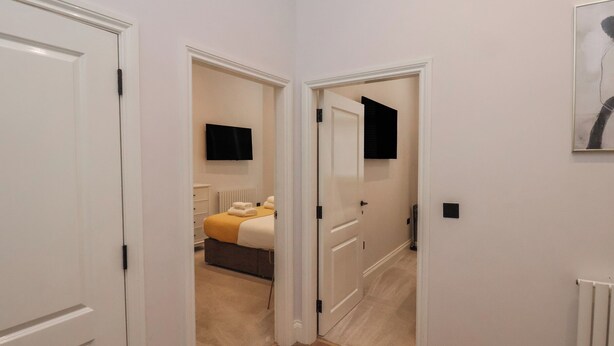 Corredor que dá para um quarto com cama, televisão e radiador.