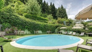 Uma piscina circular rodeada por grama verde, com espreguiçadeiras e guarda-sóis.