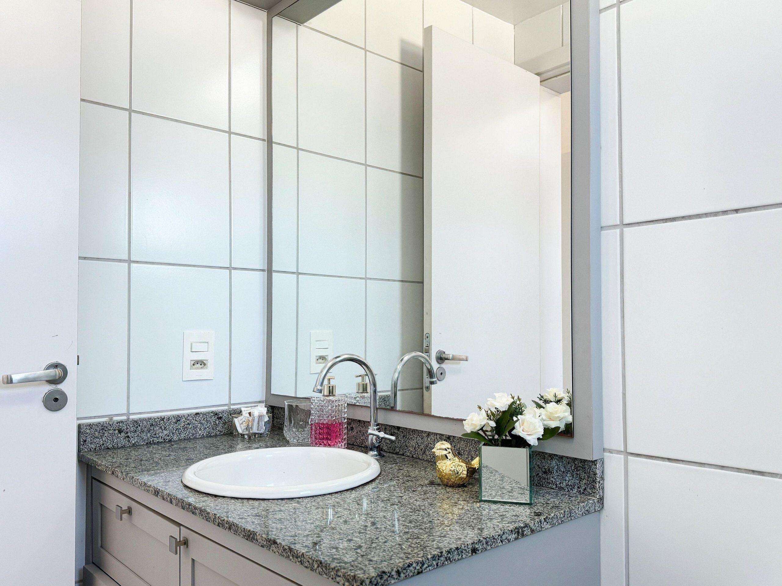 Uma casa de banho moderna com lavatório branco, bancada de granito e um espelho grande.