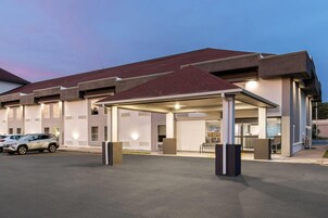 Um hotel moderno com entrada coberta, estacionamento e um edifício com várias janelas e telhado plano.