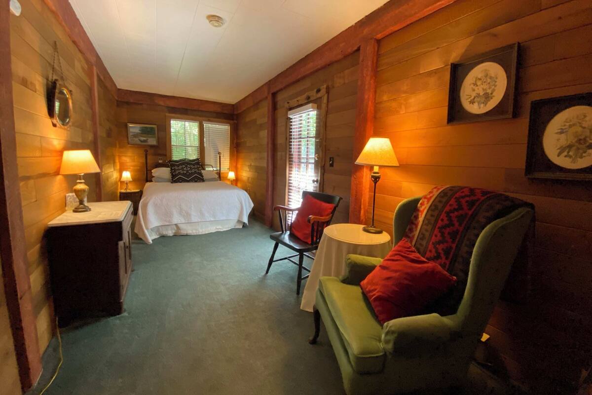 Um quarto aconchegante com uma cama, uma poltrona verde, uma mesinha e um abajur.