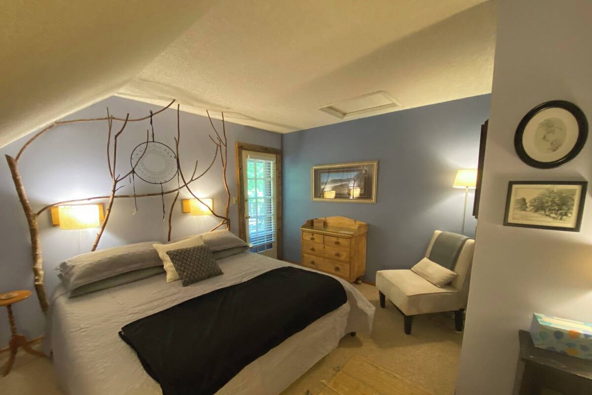 Quarto com cama, cómoda de madeira, cadeira e luminária na parede.