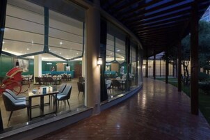 Um hall de hotel moderno com parede de vidro, piso de madeira e teto com iluminação linear.
