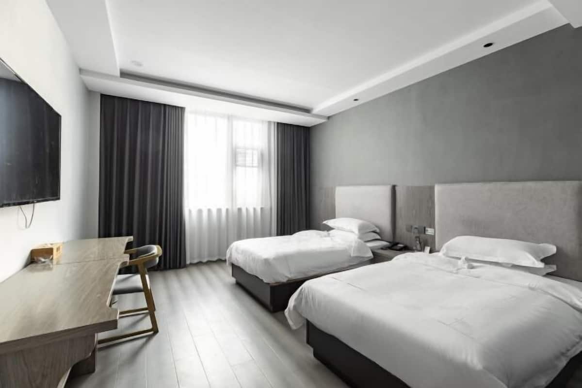 Quarto de hotel com duas camas, uma escrivaninha, televisão de tela plana e janela com cortinas.