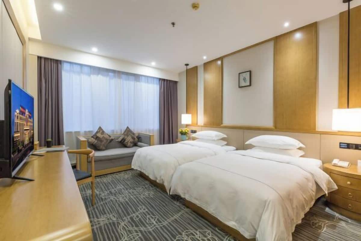 Quarto de hotel com uma cama grande, uma escrivaninha, uma televisão e uma janela com cortinas.