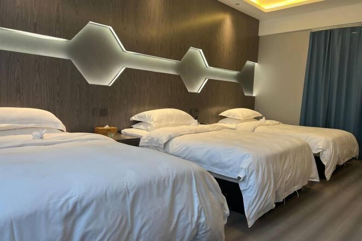 Quarto de hotel com três camas de solteiro, parede de madeira e luminária moderna.