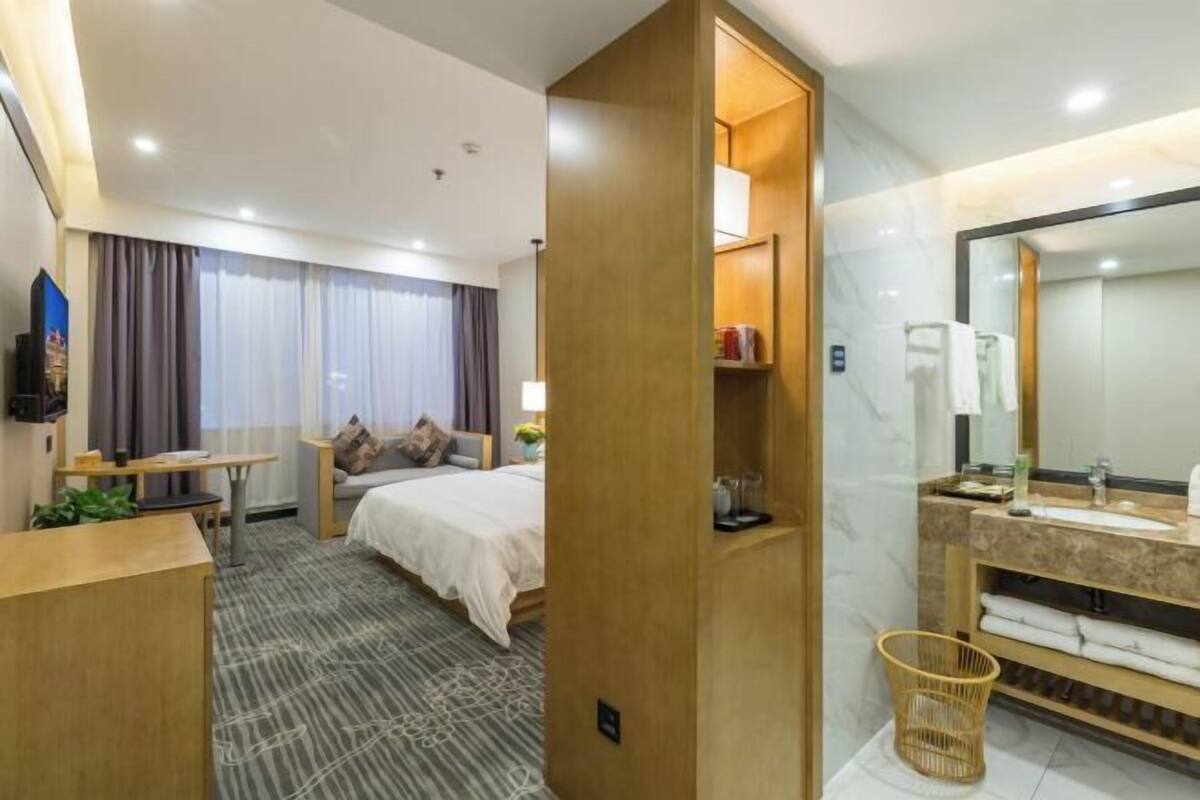 Quarto de hotel com cama, mesa de cabeceira, abajur e um espelho grande.