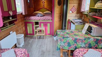Um quarto aconchegante estilo cabana, com beliche, uma mesinha e um espaço de cozinha compacto.