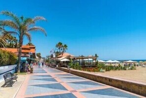 Um calçadão costeiro com palmeiras, guarda-sóis de praia e um céu azul límpido.