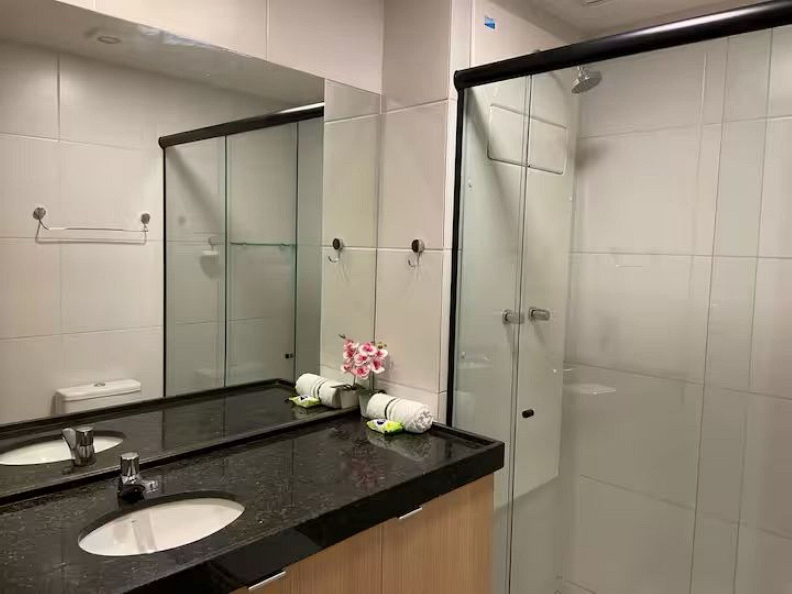 Uma casa de banho moderna com bancada preta, duas pias, um espelho grande e cabine de duche em vidro.
