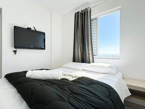 Quarto de hotel com cama, televisão de tela plana na parede, janela com cortinas e vista para a paisagem urbana.