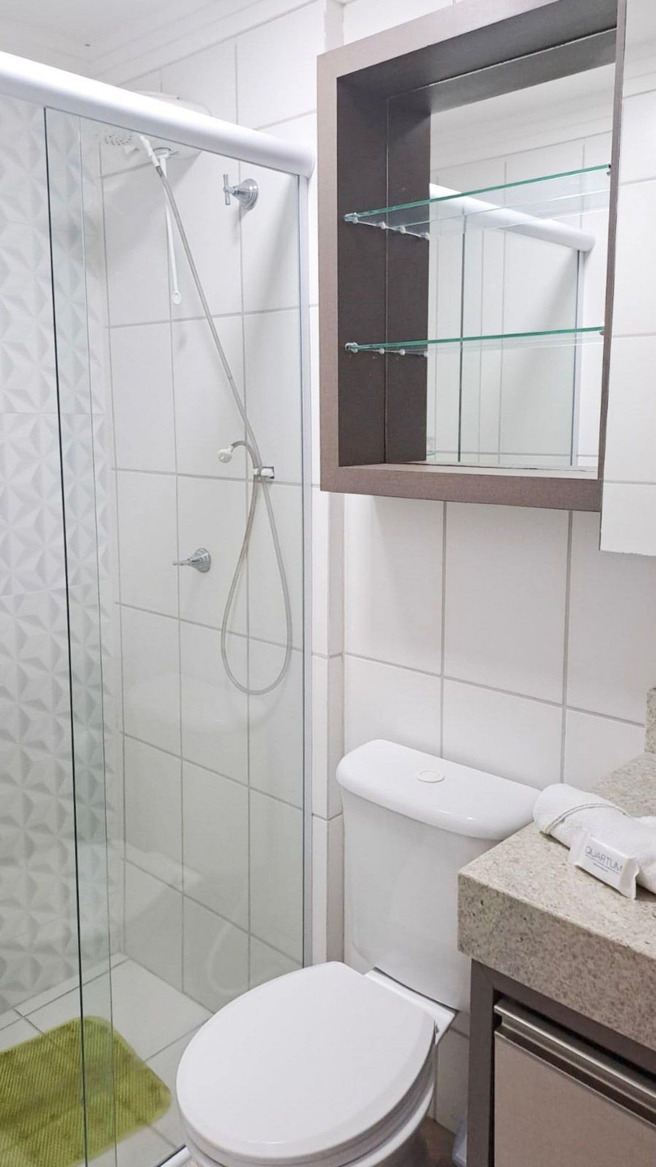 Um banheiro moderno com box de vidro, vaso sanitário branco e prateleira de vidro sobre a pia.