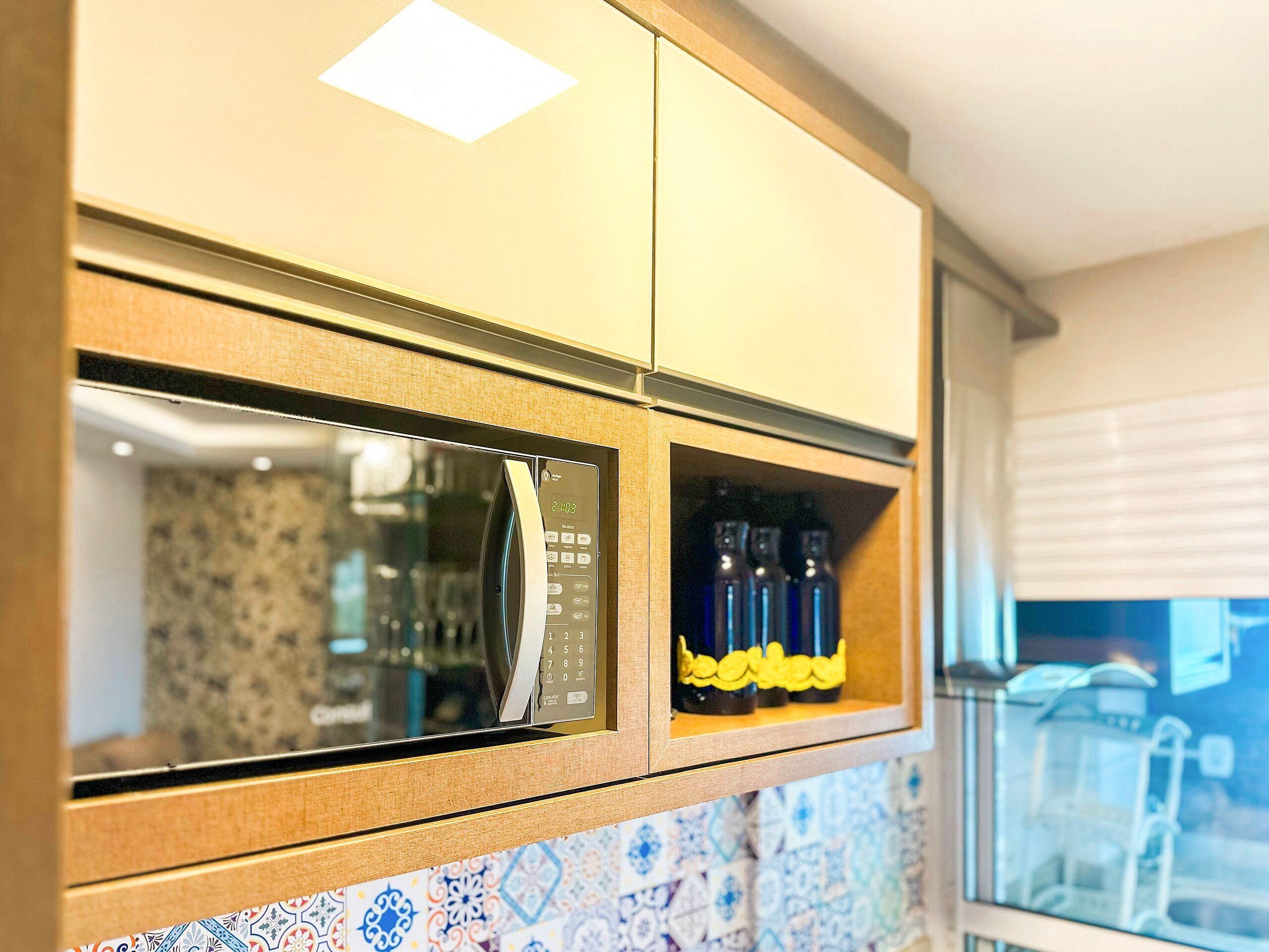 Cozinha com micro-ondas, prateleira com garrafas e painel decorativo.