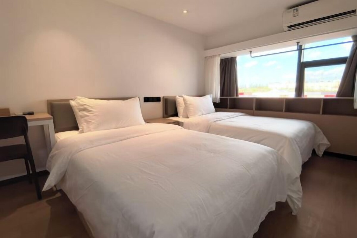 Quarto de hotel com duas camas, uma escrivaninha e janela com vista.