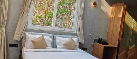 Quarto com uma cama grande, claraboia, cortinas e vista para árvores lá fora.