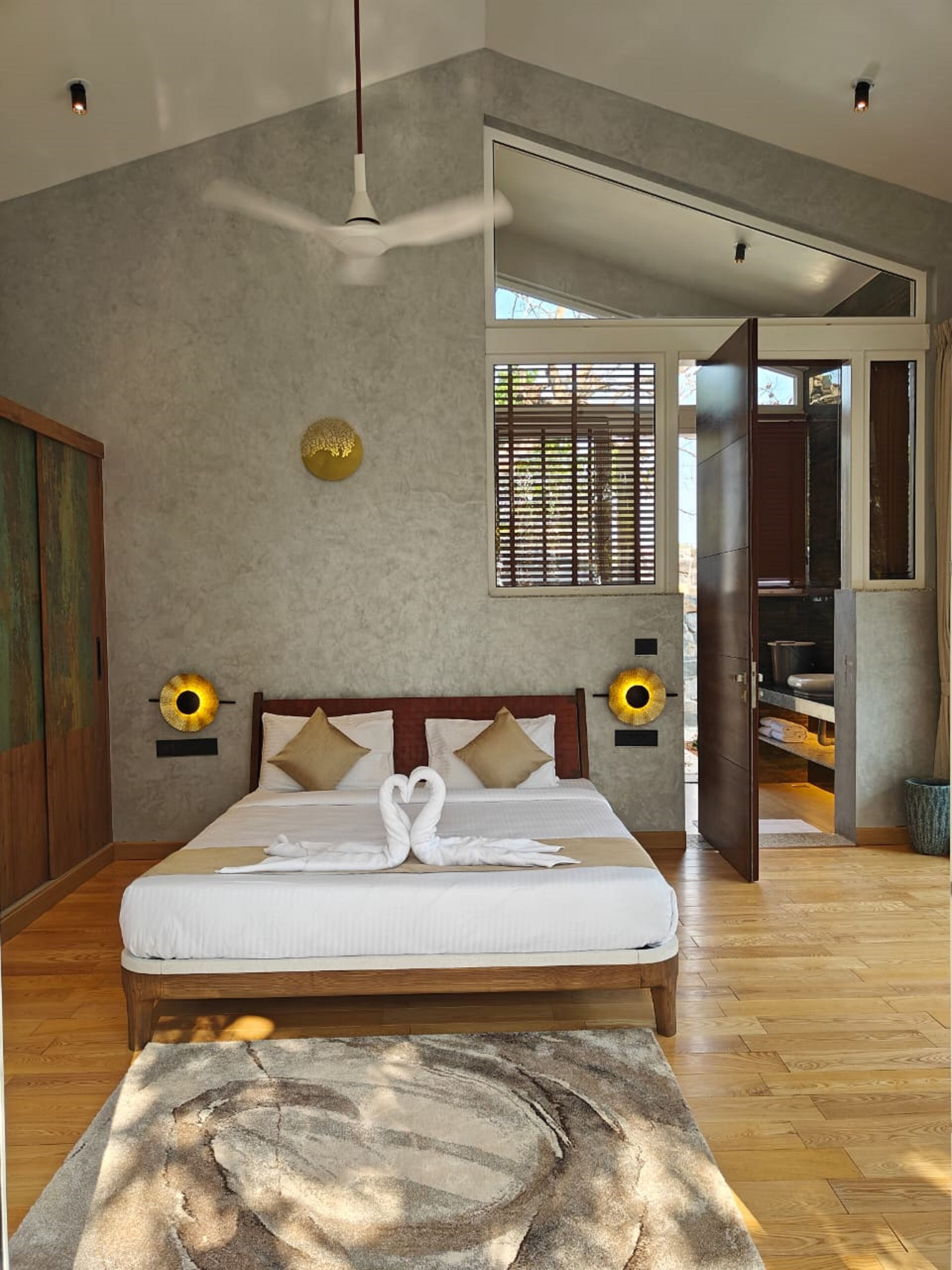 Quarto com cama grande, ventoinha no teto, janela com persianas e chão de madeira.