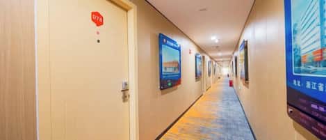Corredor de hotel com portas, piso coberto por carpete e cartazes nas paredes.