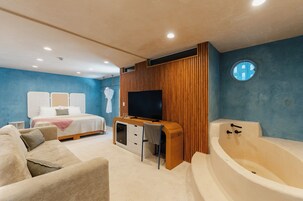 Quarto moderno com uma cama grande, TV, móvel para entretenimento de madeira, banheira e parede azul decorativa.