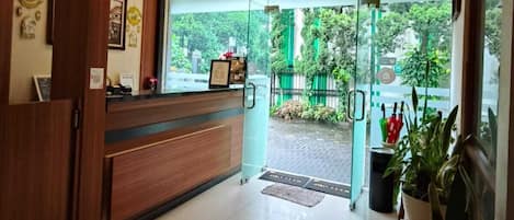 Uma área de recepção de hotel com um balcão de madeira, uma porta de vidro que dá para o exterior e um chão de azulejos.
