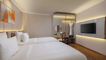 Quarto de hotel com duas camas, uma escrivaninha, uma cadeira, uma televisão e um espelho.