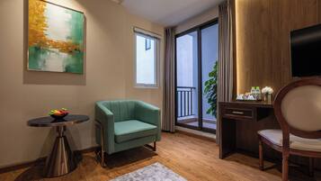 Quarto de hotel moderno com poltrona verde, escrivaninha, televisão de tela plana, um quadro, uma janela e varanda com planta.
