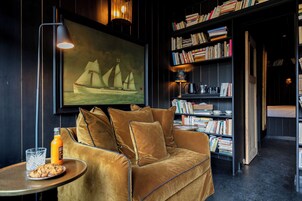 Um quarto aconchegante com um sofá de veludo, uma estante de livros e um quadro de um navio a vela.