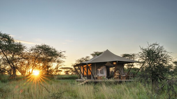 Acomodação em tenda com cama, área de estar e vista para o pôr do sol.