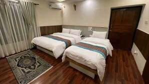 Quarto de hotel com duas camas, piso de madeira, tapete estampado e uma porta.
