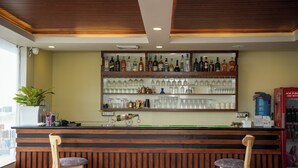 Uma área de bar com painéis de madeira, diversos frascos de bebidas alcoólicas e dois bancos.