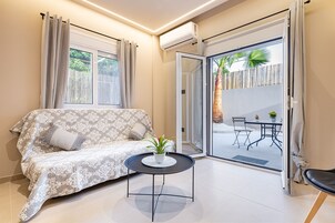 Uma sala de estar moderna com sofá, uma mesinha redonda com uma planta e uma porta de vidro deslizante para um pátio externo.