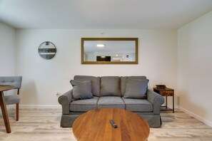 Uma sala de estar com um sofá cinzento, uma mesa de centro redonda de madeira, um espelho redondo e uma pequena mesinha lateral.