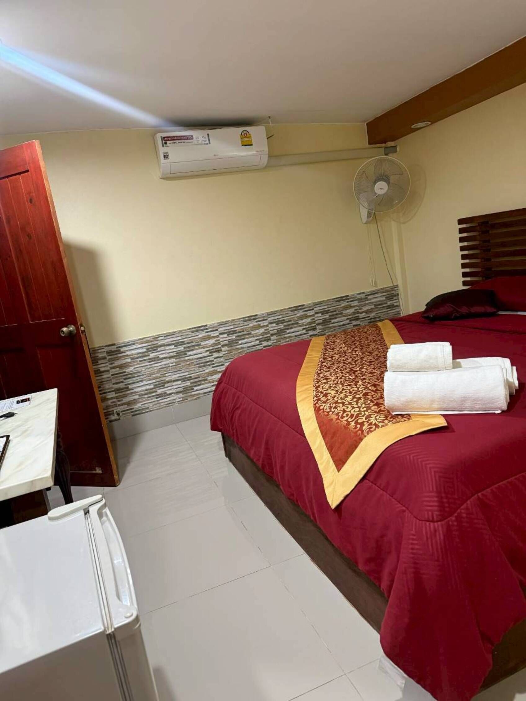 Quarto de hotel com uma cama, uma escrivaninha, uma cadeira, ar-condicionado e ventoinha na parede.