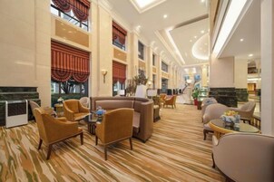 Um hall de hotel com teto alto, um balcão de recepção de mármore e uma área de estar com sofás e poltronas.
