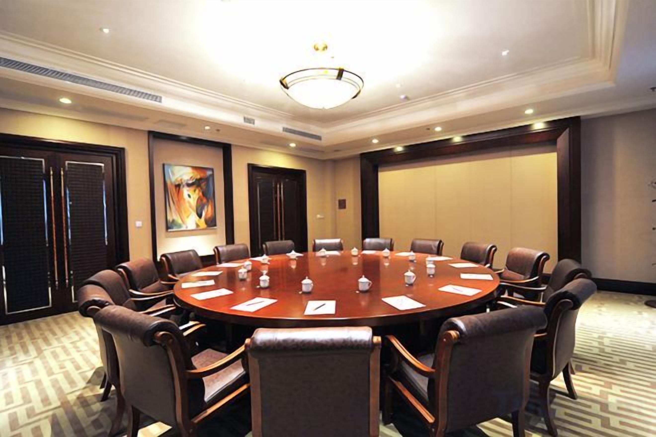 Uma sala de conferências com uma mesa redonda, cadeiras e uma tela de projeção.