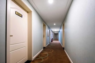 Corredor de hotel com portas, piso coberto por carpete e teto em tom claro.