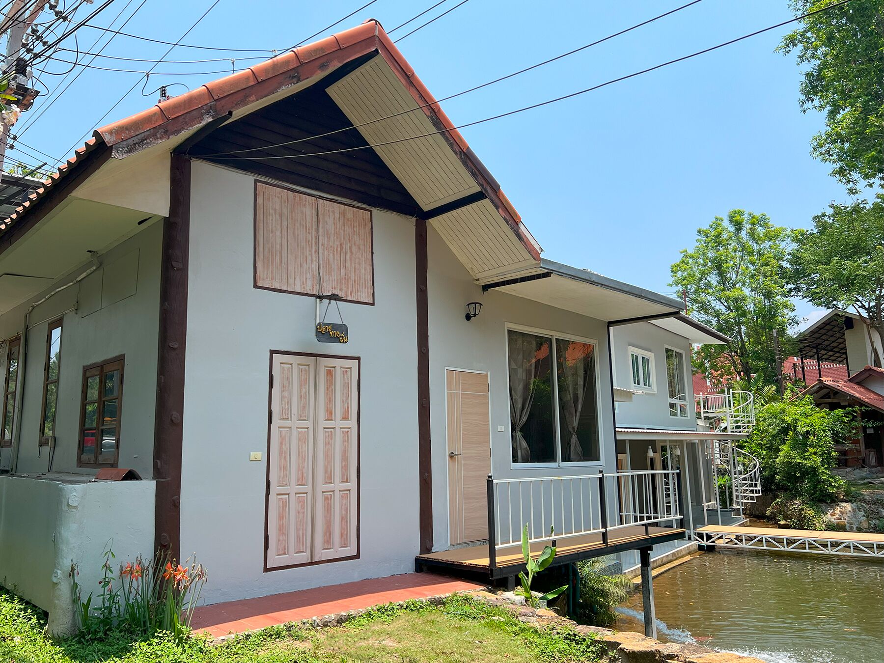 Uma casa de dois andares com varanda, um pequeno lago e um deck de madeira.