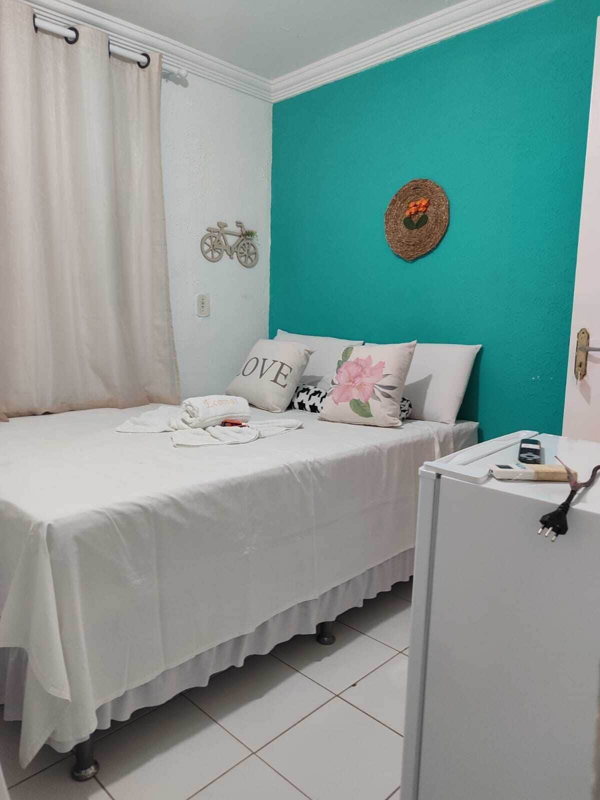 Quarto pequeno e bem organizado, com cama, guarda-roupa branco e parede de destaque em tom de verde-água.