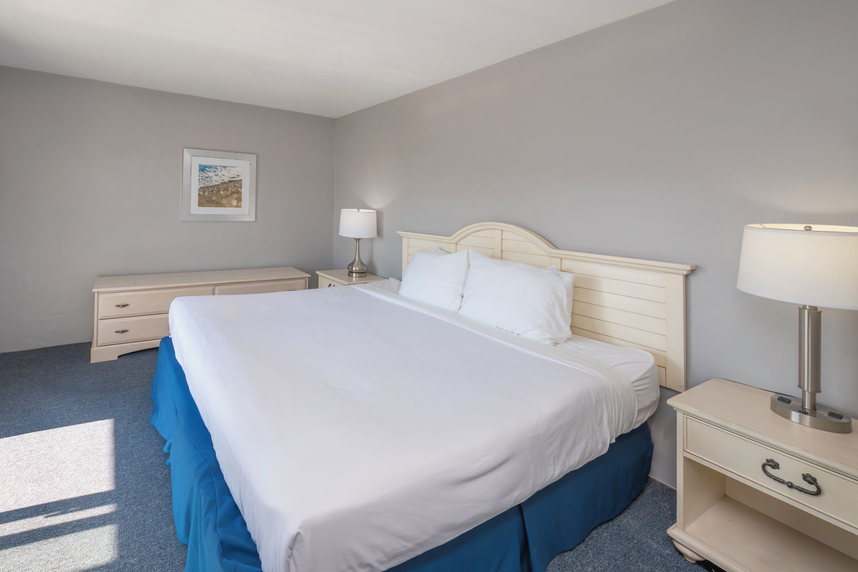 Quarto bem arrumado com cama, mesas de cabeceira e um quadro na parede.