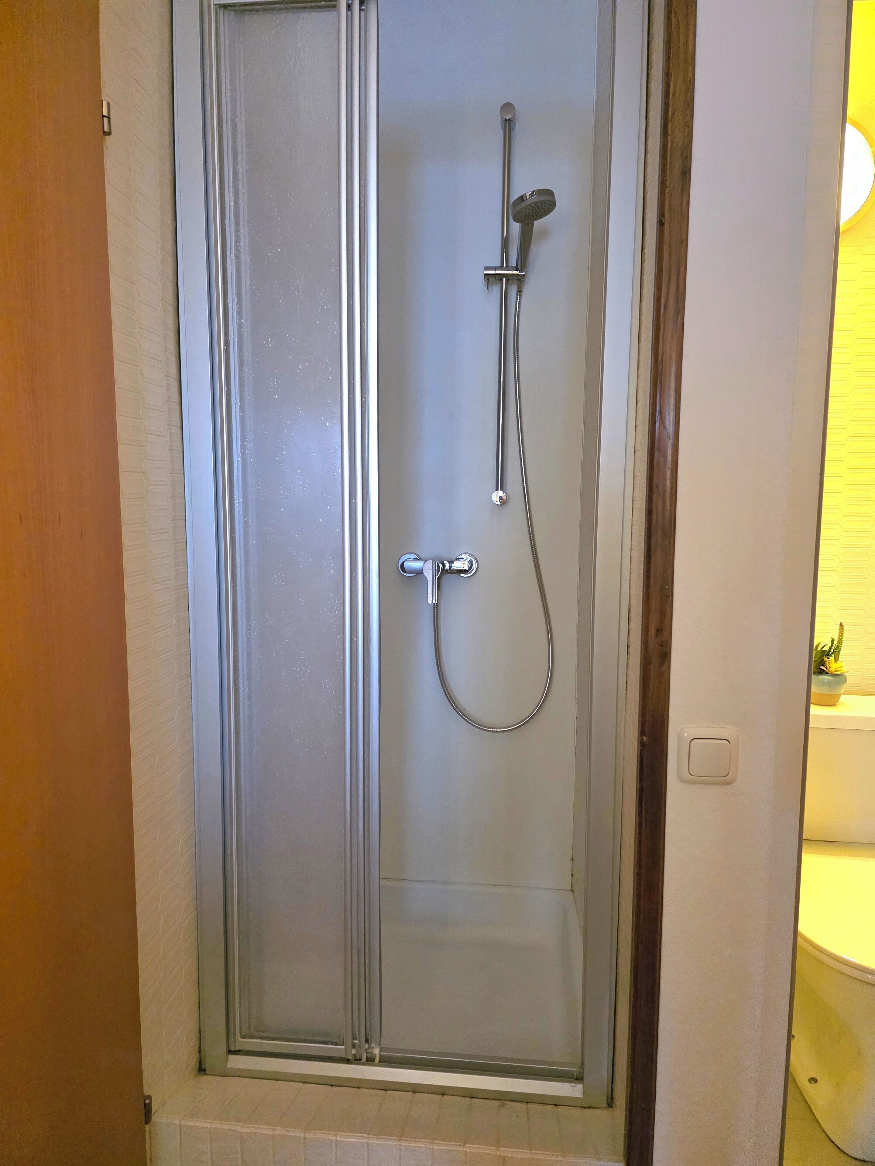 Um chuveiro com divisória de vidro, um chuveiro manual e uma torneira fixada na parede.