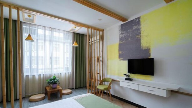 Quarto de hotel com uma cama, uma escrivaninha, uma cadeira, uma televisão e uma janela grande com cortinas.