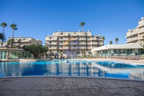 Piscina com céu azul límpido, cercada por palmeiras e edifícios modernos.