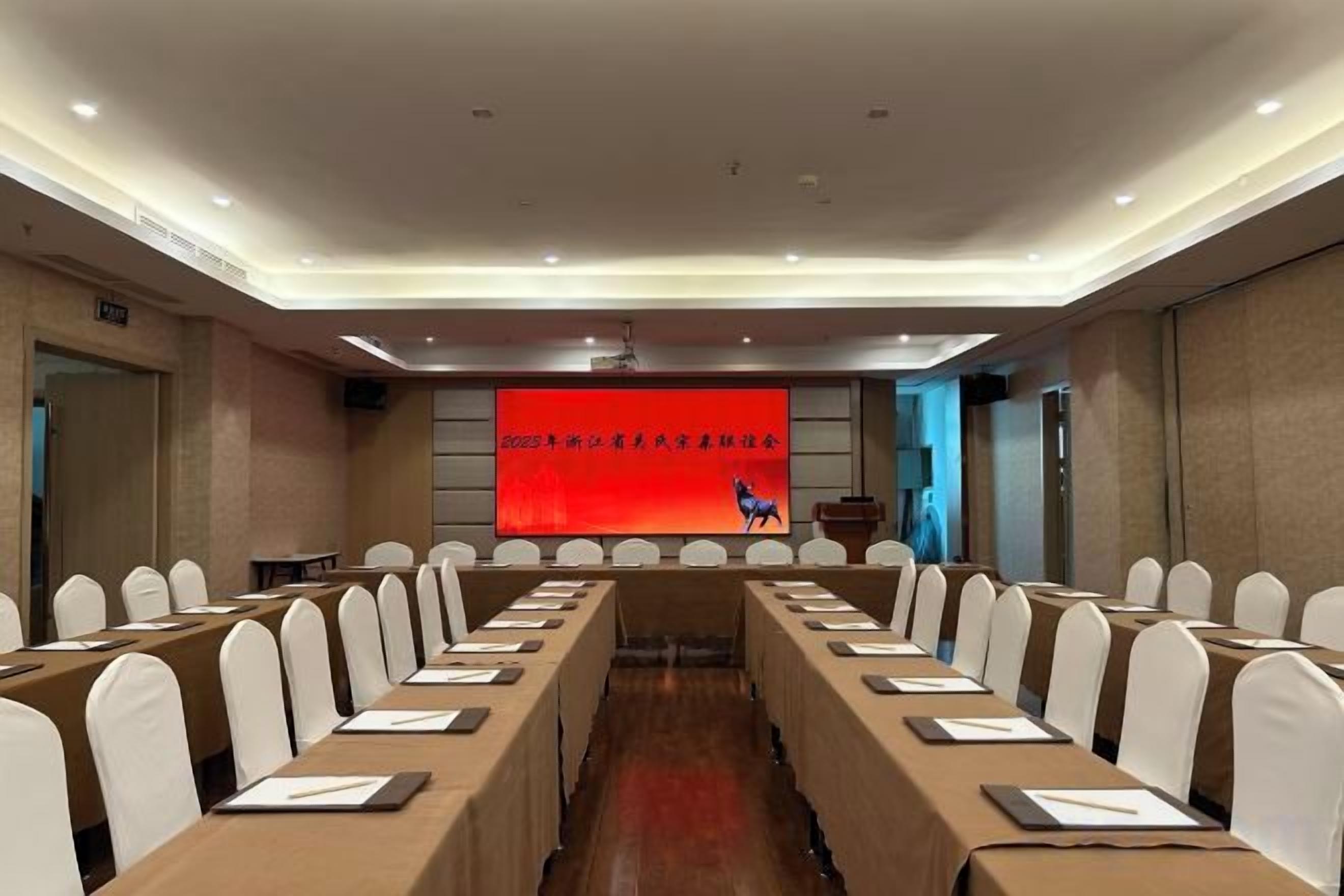 Sala de conferências com mesas grandes, cadeiras e tela de projeção.