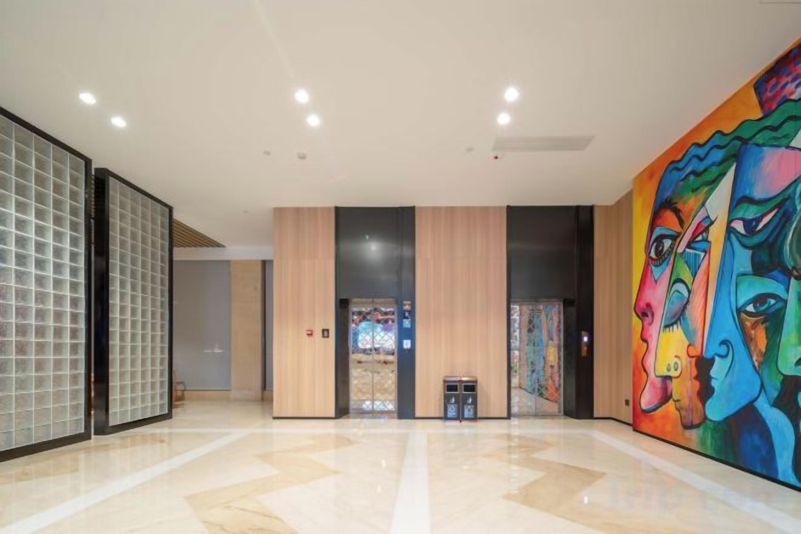 Um hall espaçoso com piso de mármore, divisória de vidro e uma pintura abstrata colorida na parede.