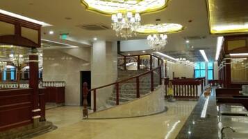 Um hall amplo com piso de mármore, uma escadaria imponente e um lustre.