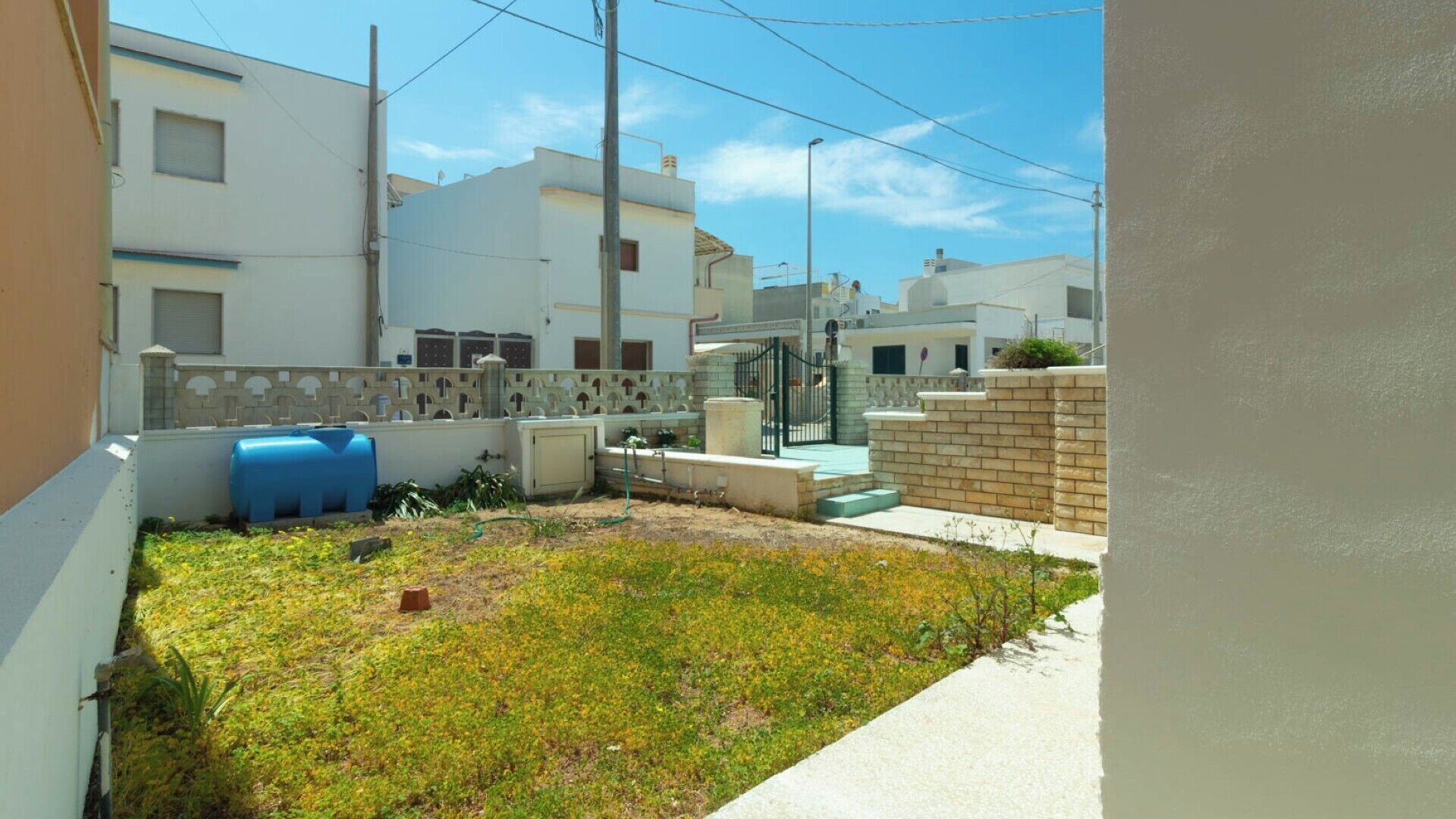 Um bairro residencial com um pequeno jardim, um reservatório de água azul e um portão.