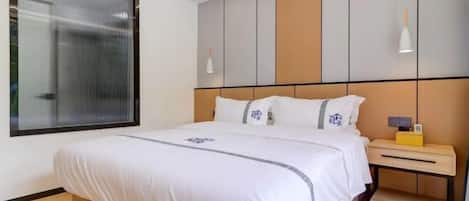 Quarto de hotel com uma cama grande, mesa de cabeceira com abajur e janela com persianas.