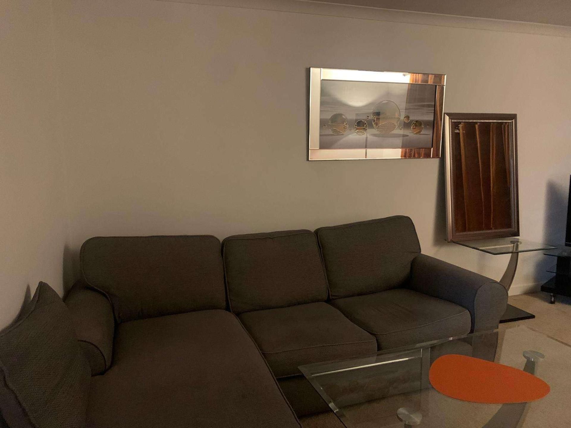 Uma sala de estar com sofá, mesa de centro de vidro e uma pintura na parede.