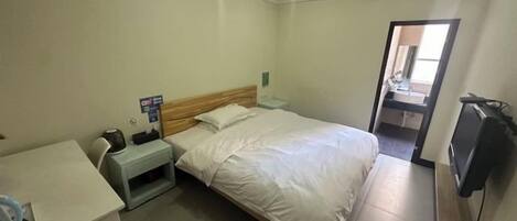 Quarto de hotel com cama, escrivaninha, mesa de cabeceira e televisão.