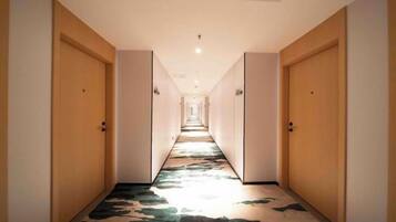 Corredor de hotel com portas em ambos os lados, piso coberto de carpete e luminária no teto.